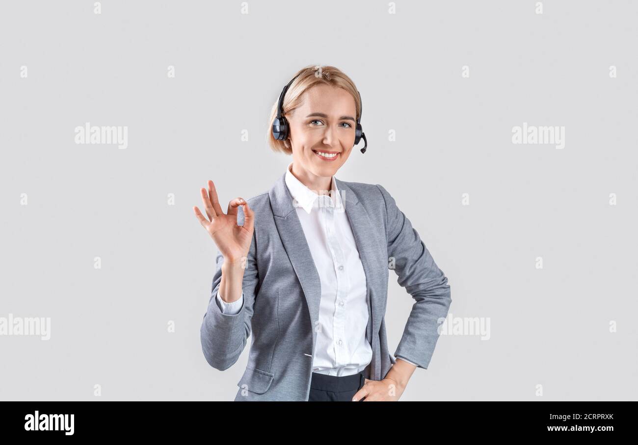 Happy call centre operator with headset showing okay gesture on light ...