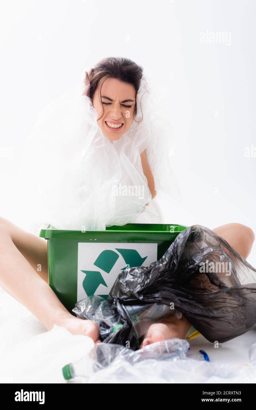 barefoot woman with migraine wrapped in plastic bag sitting near trash ...