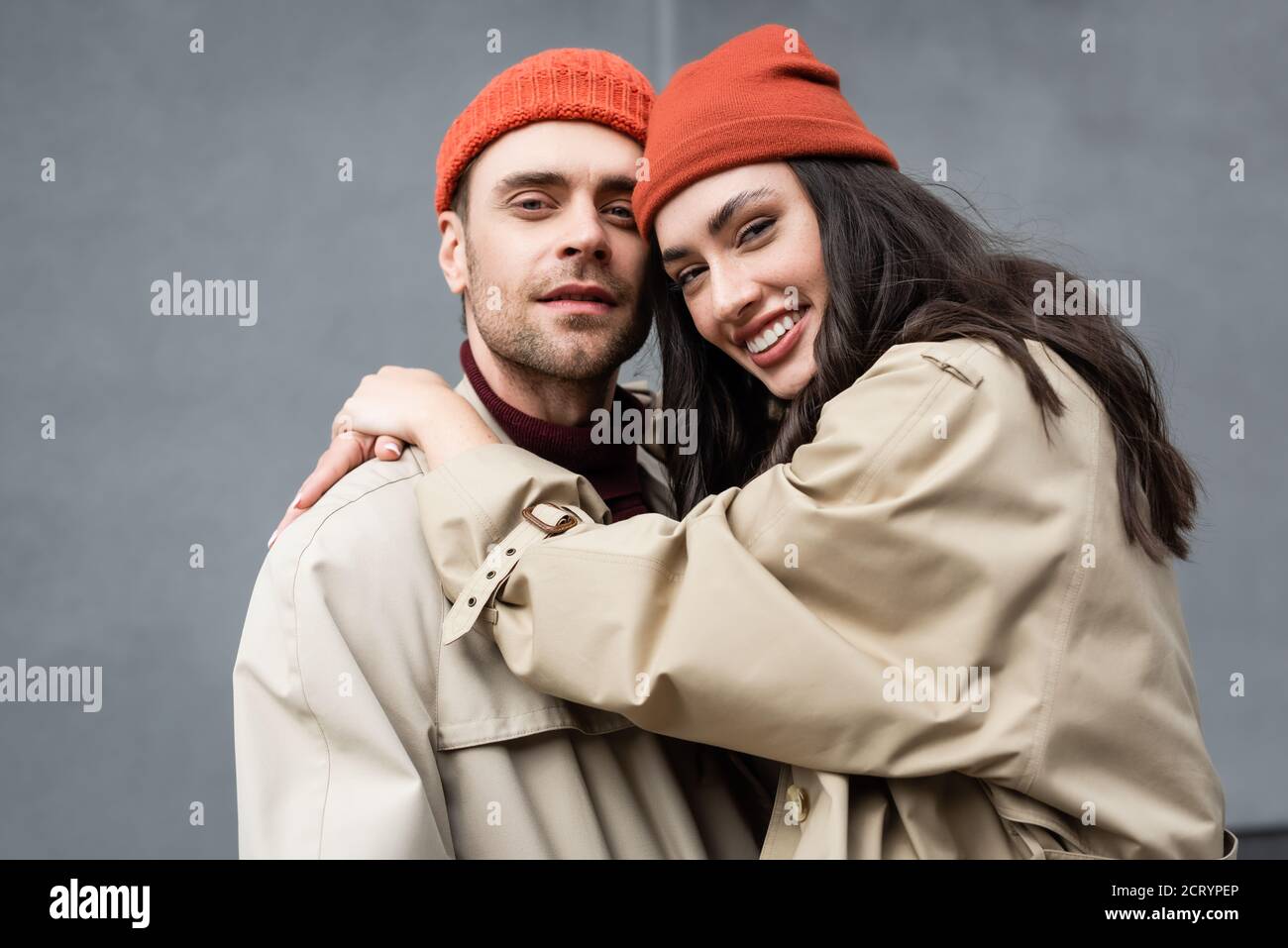 trendy woman in beanie hat hugging man in trench coat Stock Photo - Alamy