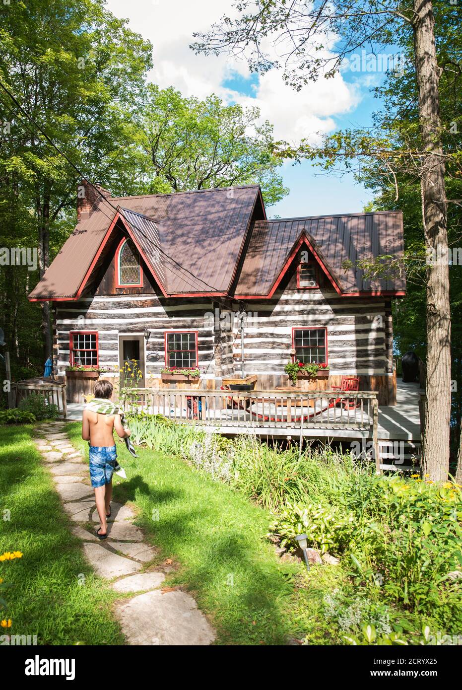 Boy walking down a path to a log cabin cottage on a summer day Stock ...