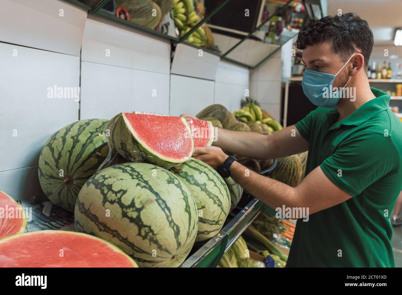 A young man wearing a mask placing watermelons in the fruit shop ...