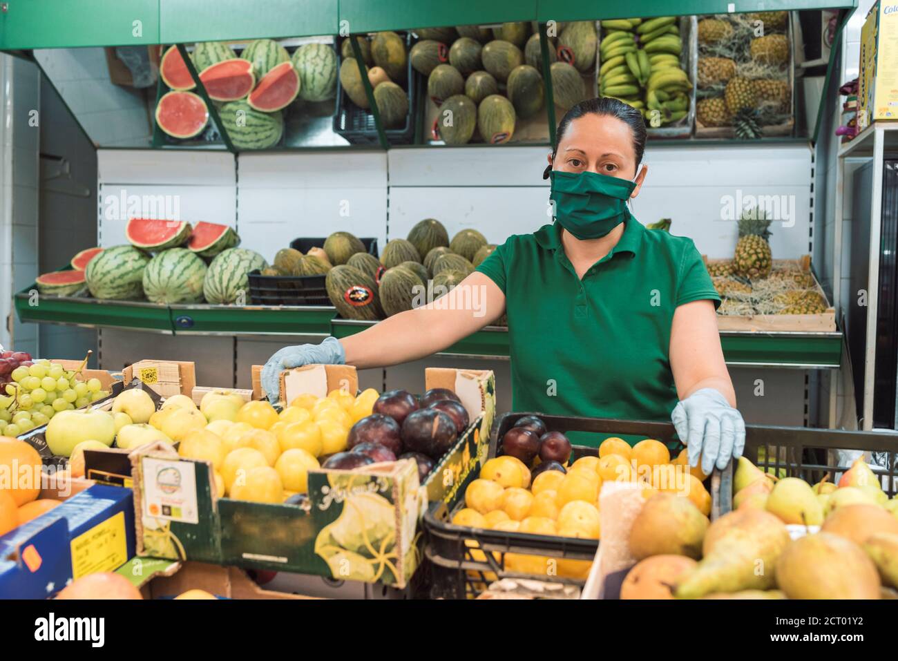 a shopkeeper with a mask poses in front of her fruit shop store concept ...