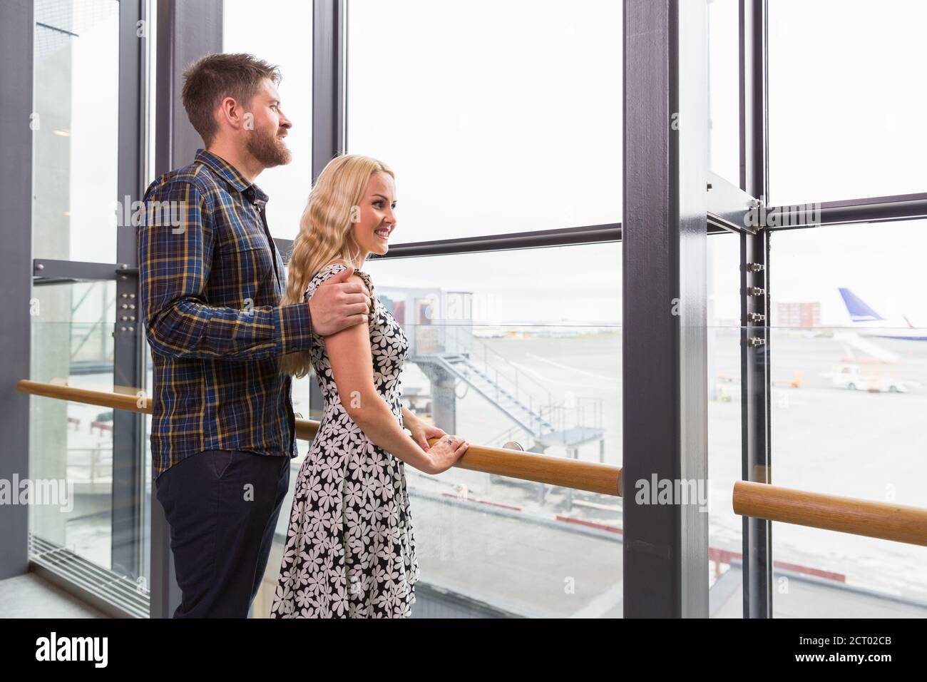 Young couple looking at airplanes through airport window while waiting ...