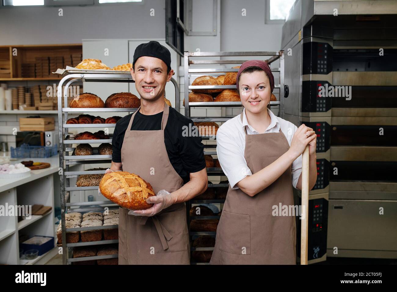 Two bakers, male and female posing for a photo in a bakery kitchen ...