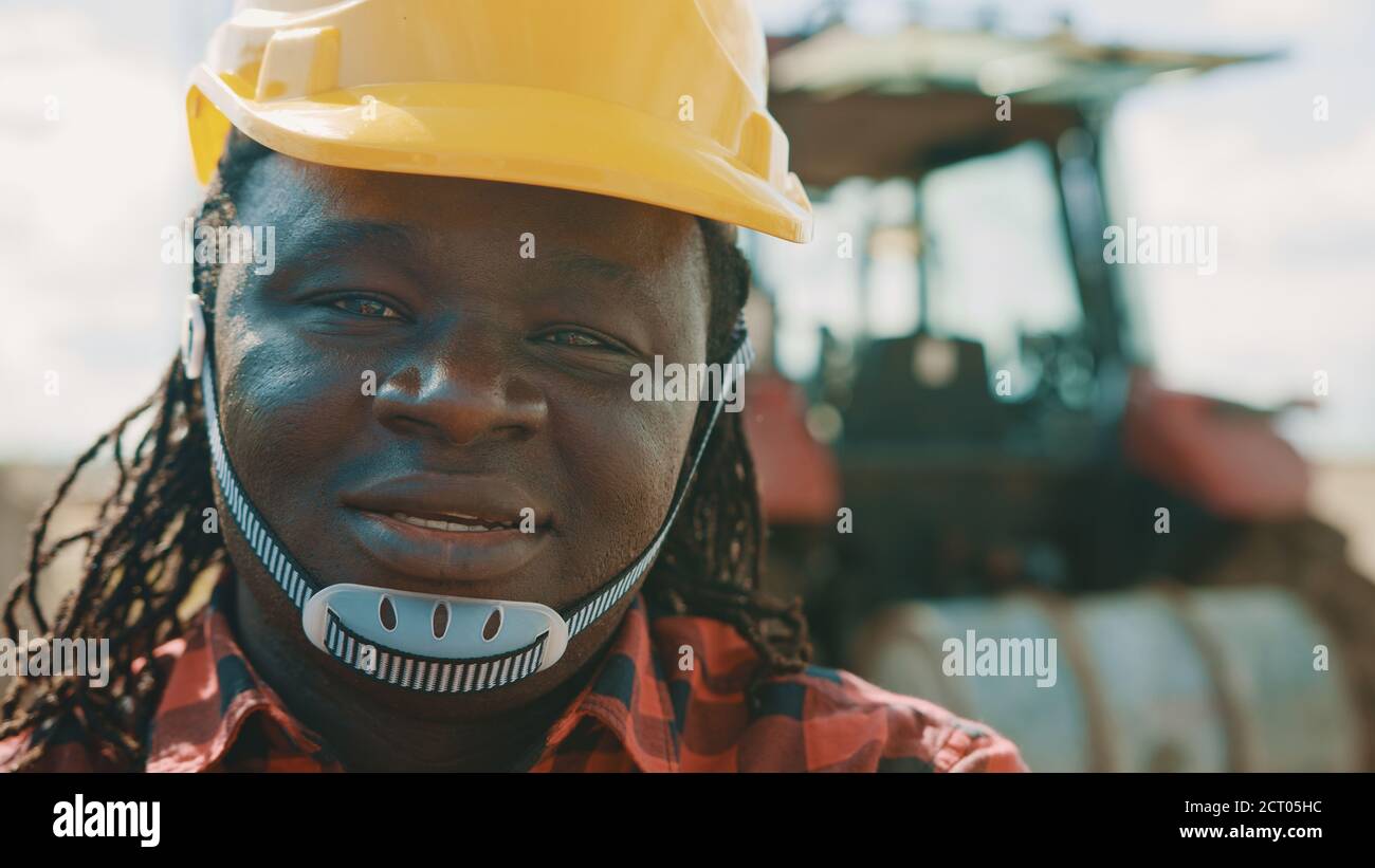 Portrait of african man with safety helmet on the farm. Tractor in the ...