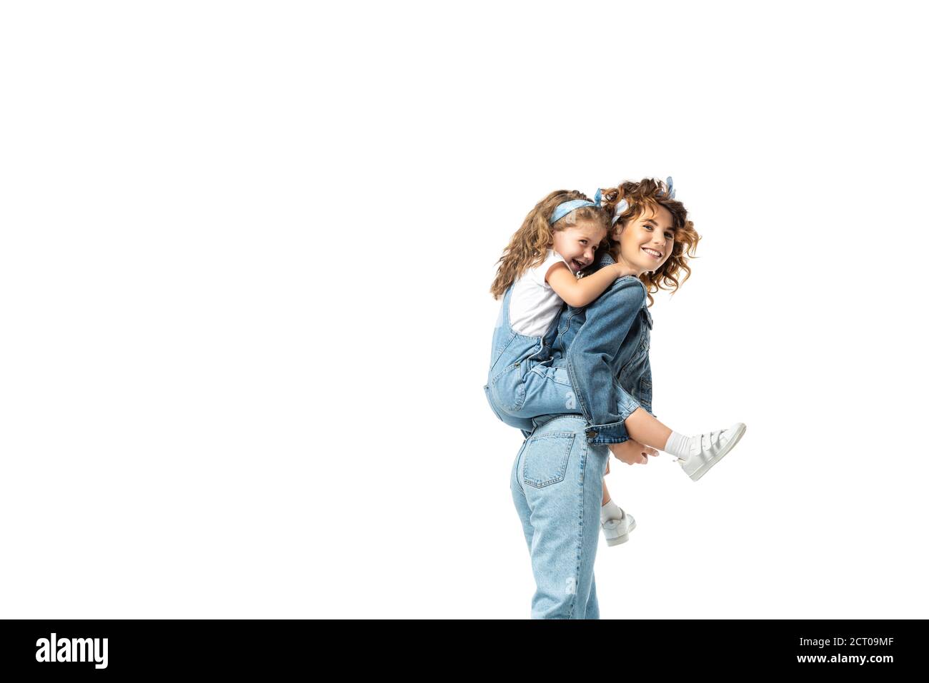 side view of mother piggybacking daughter in denim outfit isolated on ...