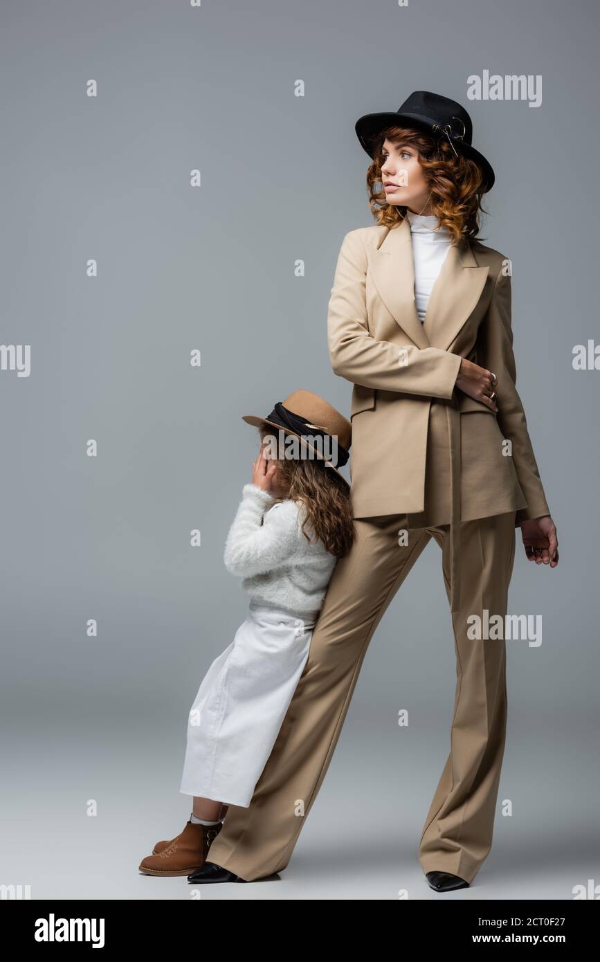 elegant mother and daughter in white and beige outfits posing on grey ...