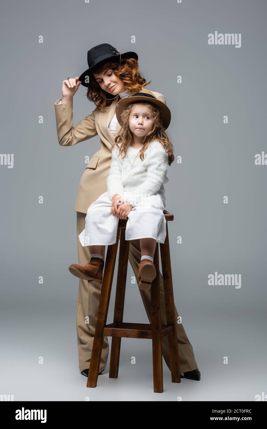elegant mother posing near daughter on chair on grey Stock Photo - Alamy