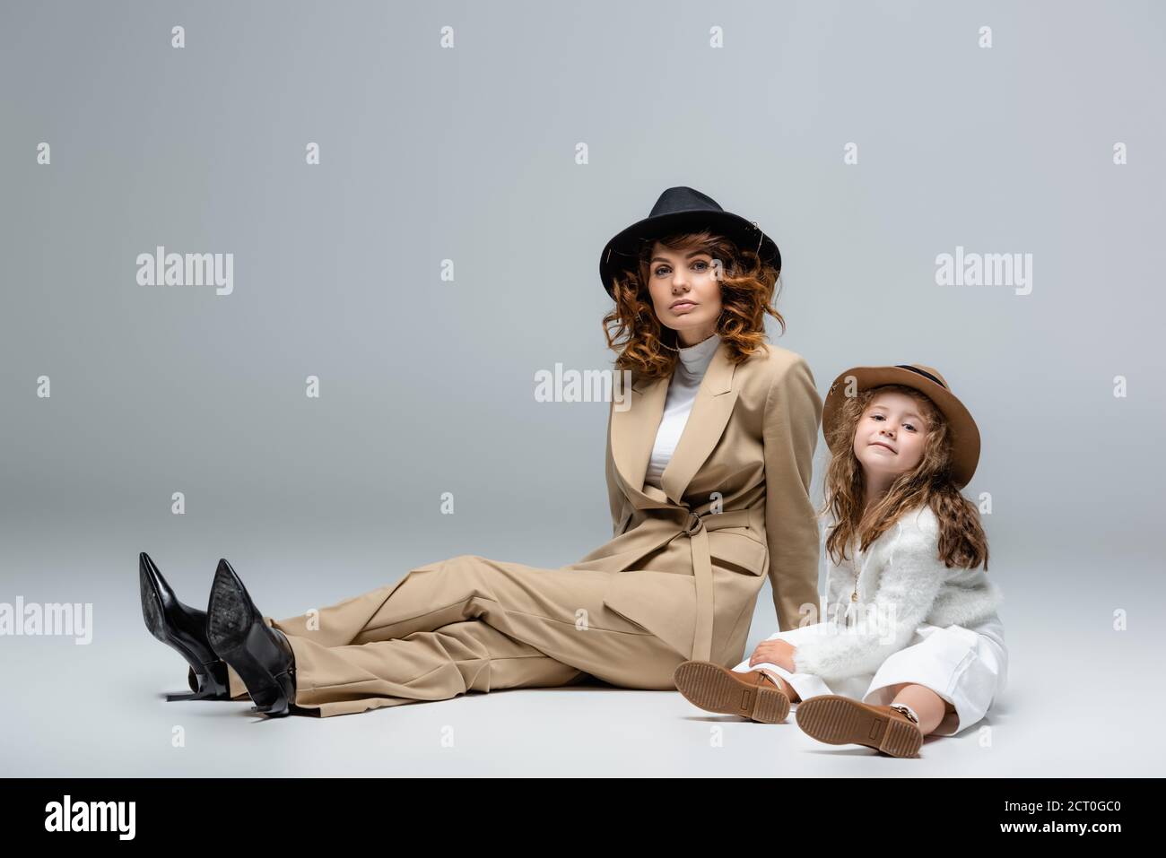elegant mother and daughter in white and beige outfits and hats posing ...
