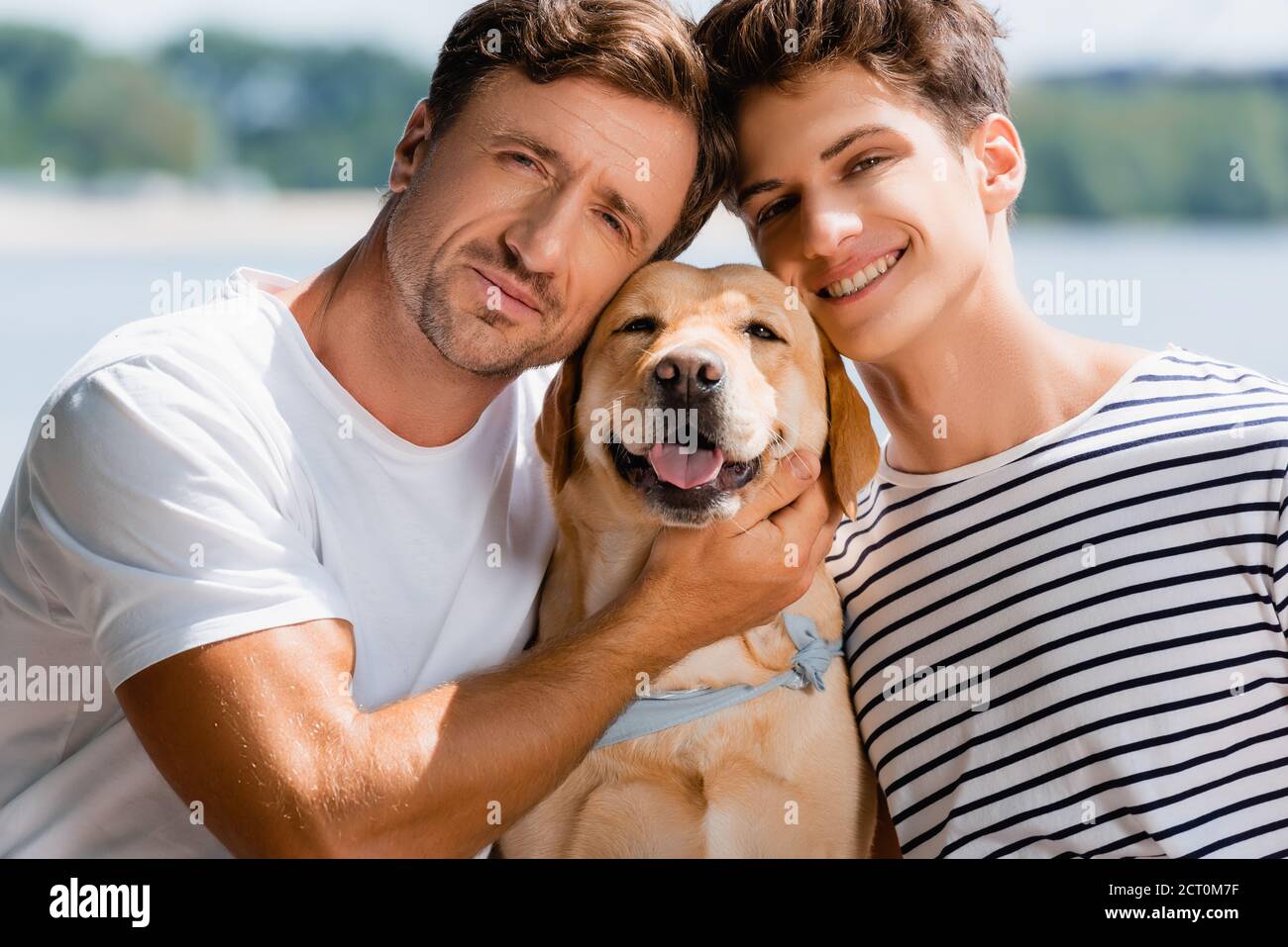 father and son looking at camera and hugging golden retriever Stock ...