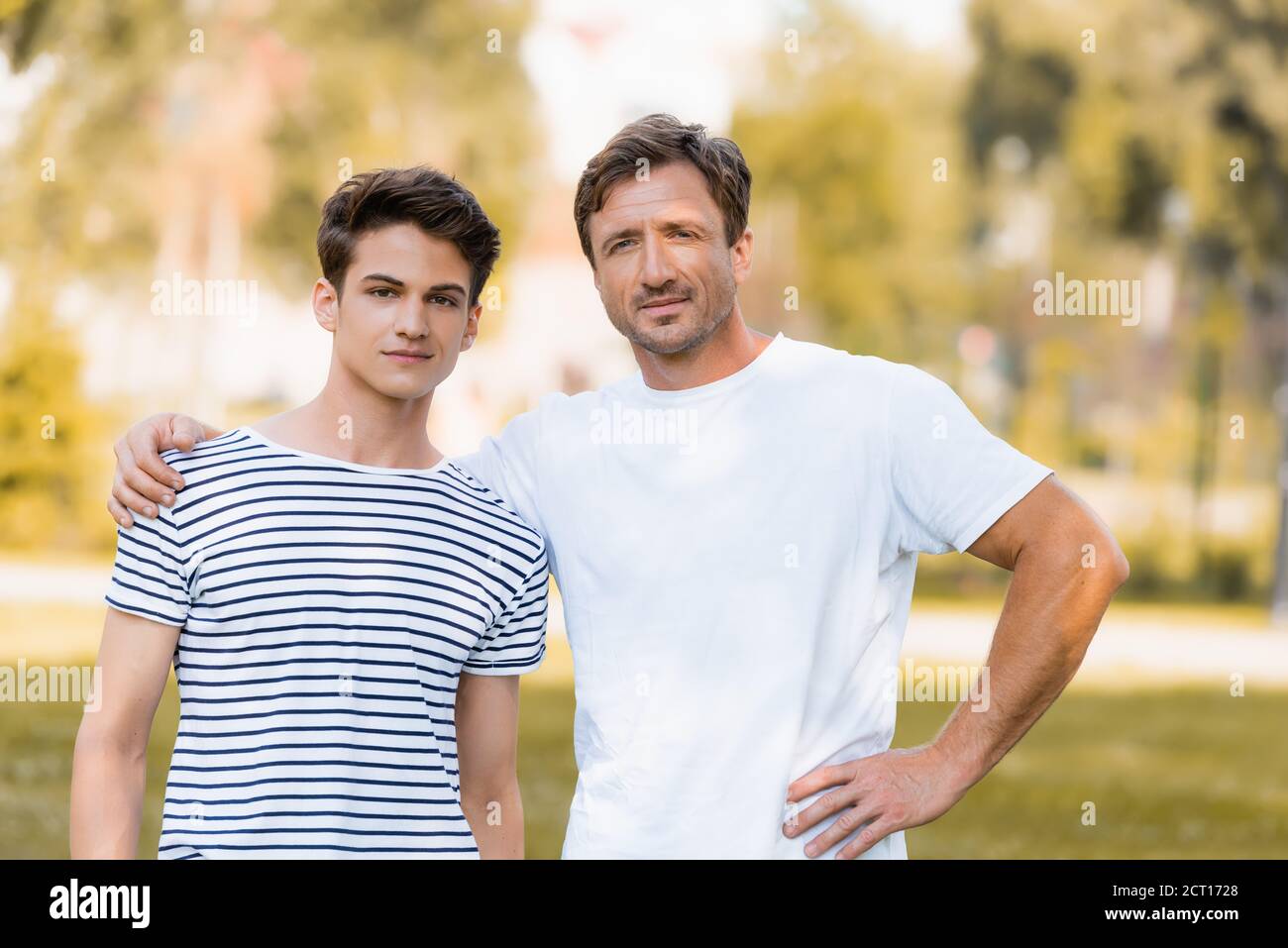 father standing with hand on hip and hugging teenager son outside Stock ...