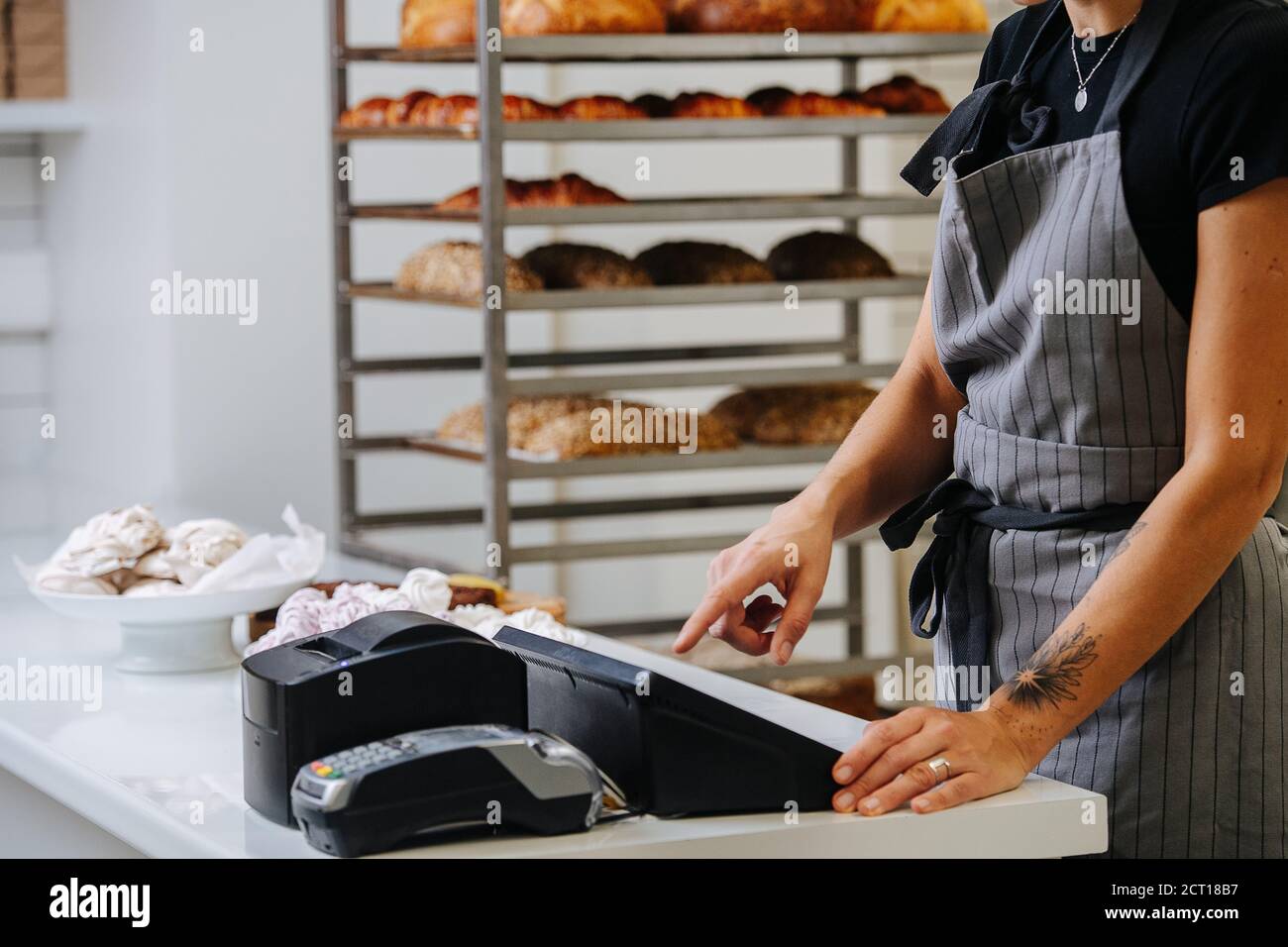 Shopkeeper standing behing cash register calculating overal cost of the ...