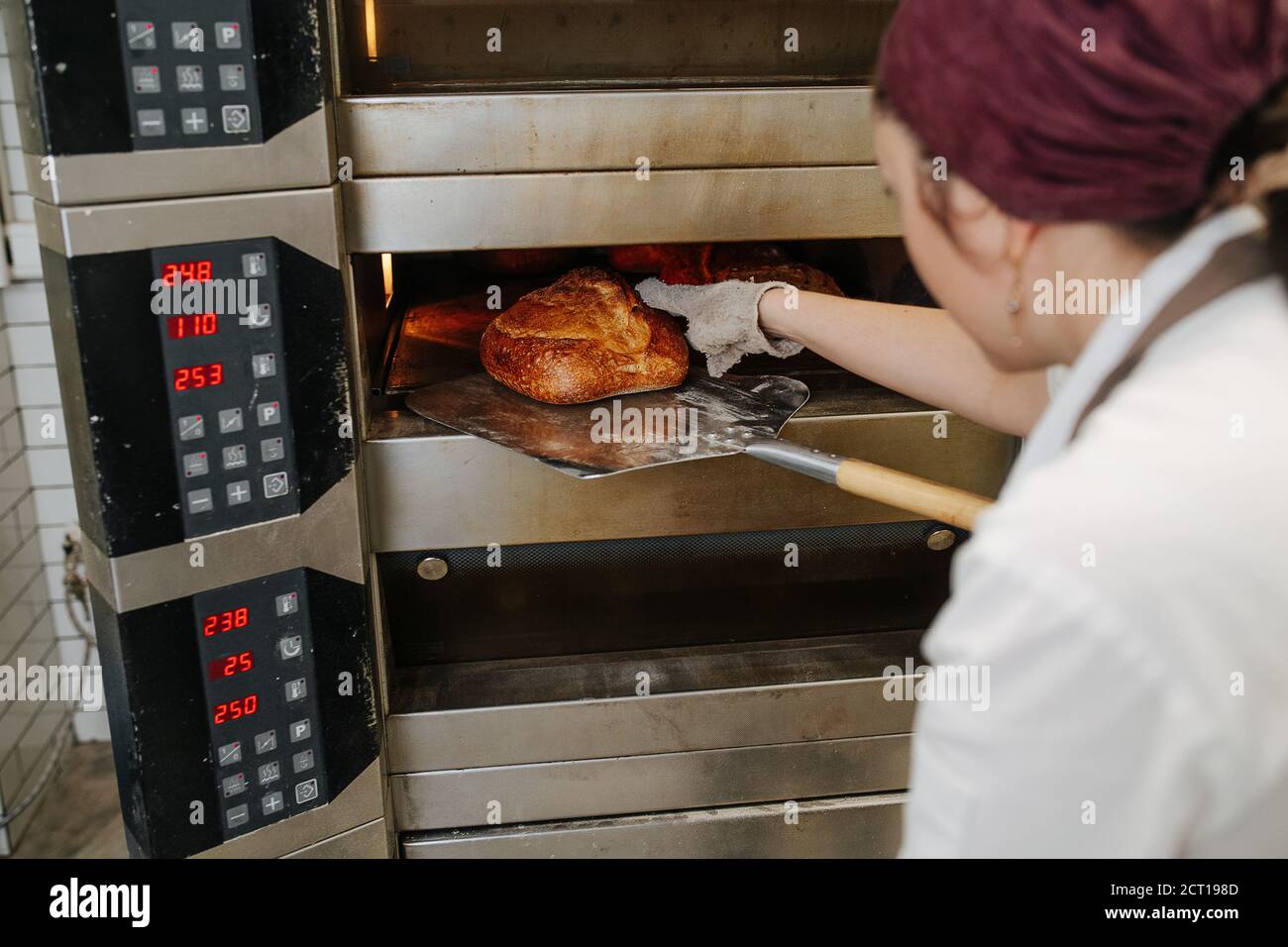 Focused female baker taking bread from oven furnace with special flat ...