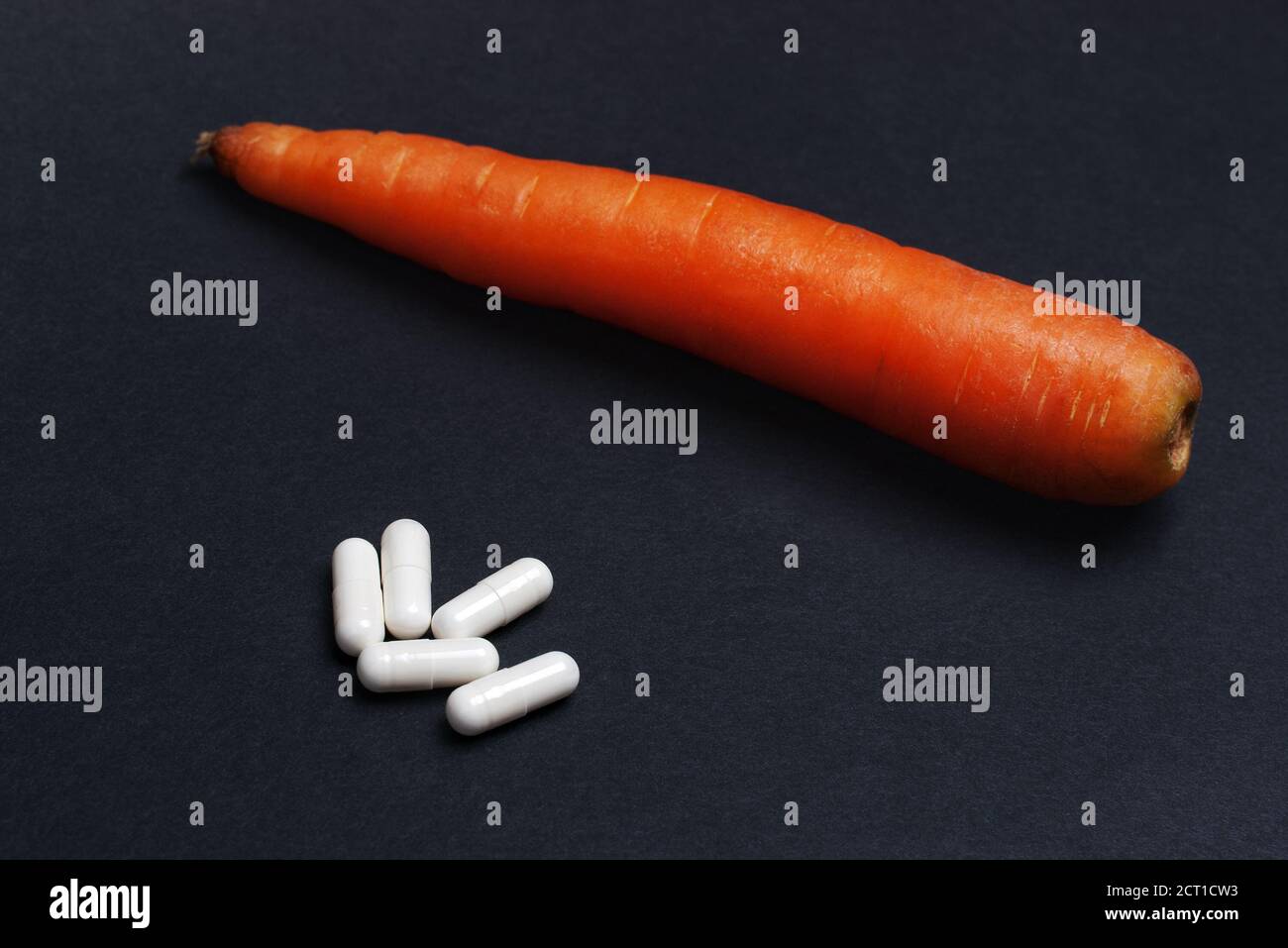 White enteric-coated tablets and a whole raw carrot on black textured ...