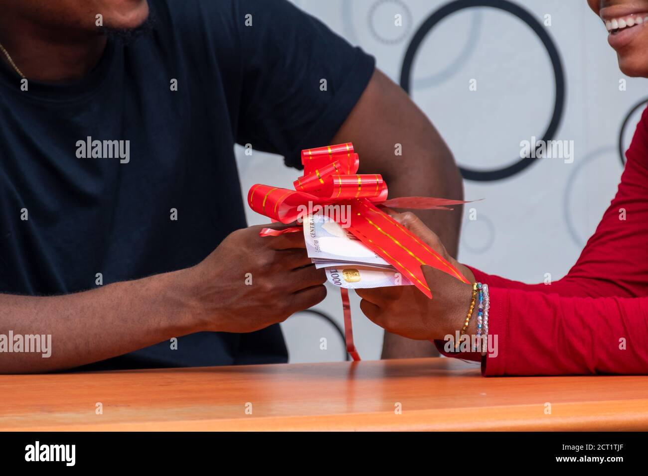 young black man giving a lady a gift of cash, wrapped with a red ribbon ...