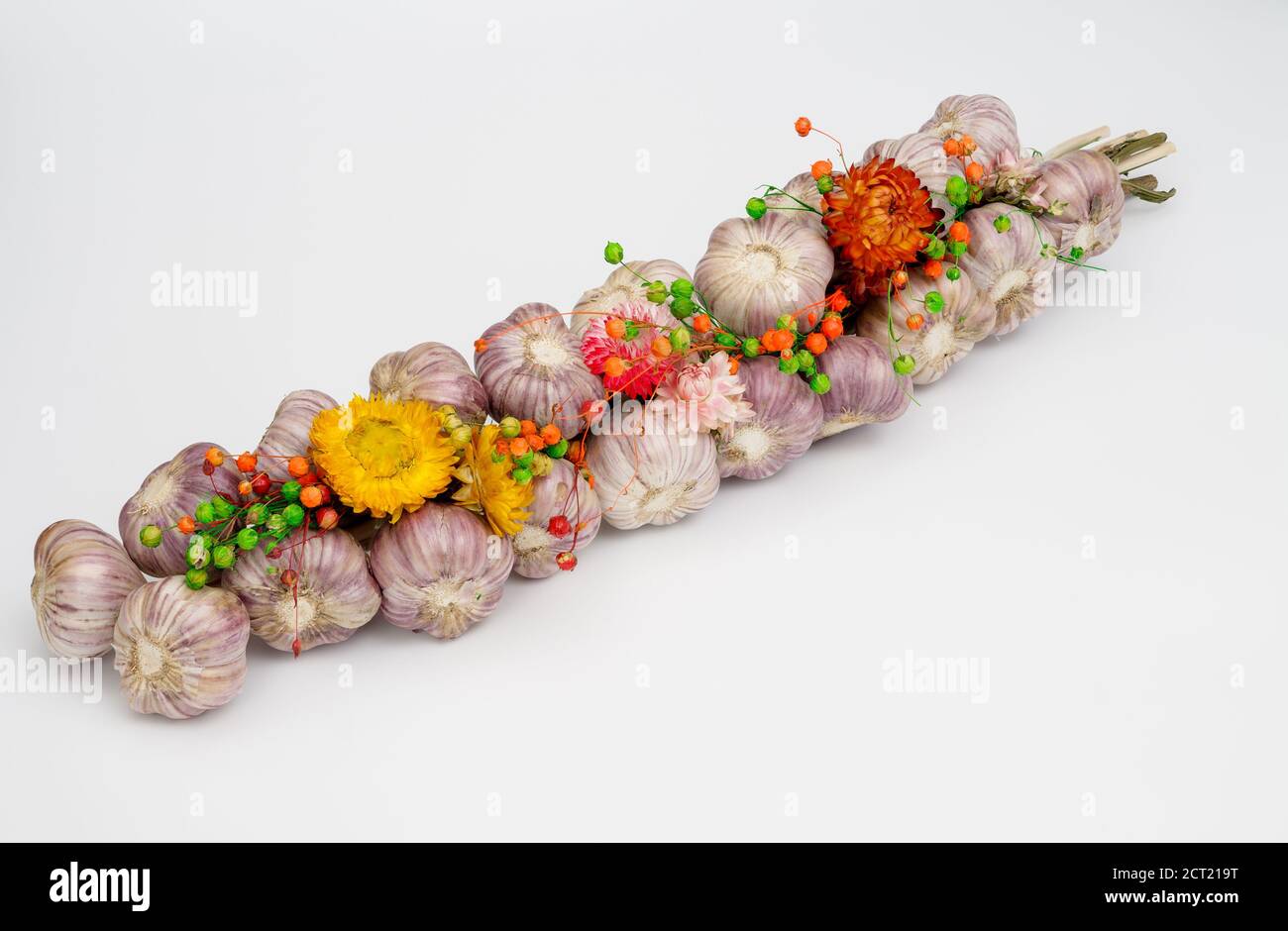 a braid of garlic, decorated with flowers, against a light background ...
