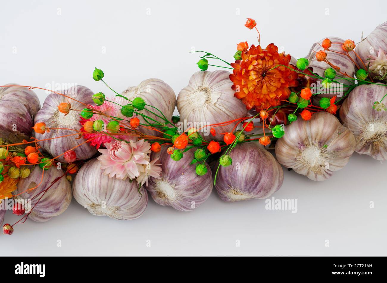 a braid of garlic, decorated with flowers, against a light background ...