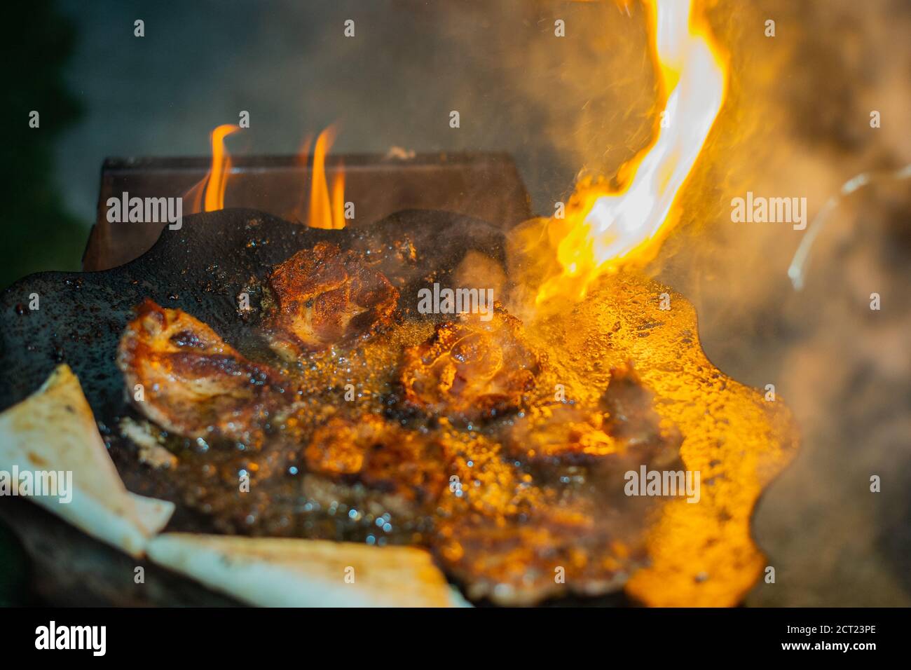 Fresh cut bacon being cooked over a campfire. Meat in a frying pan over ...