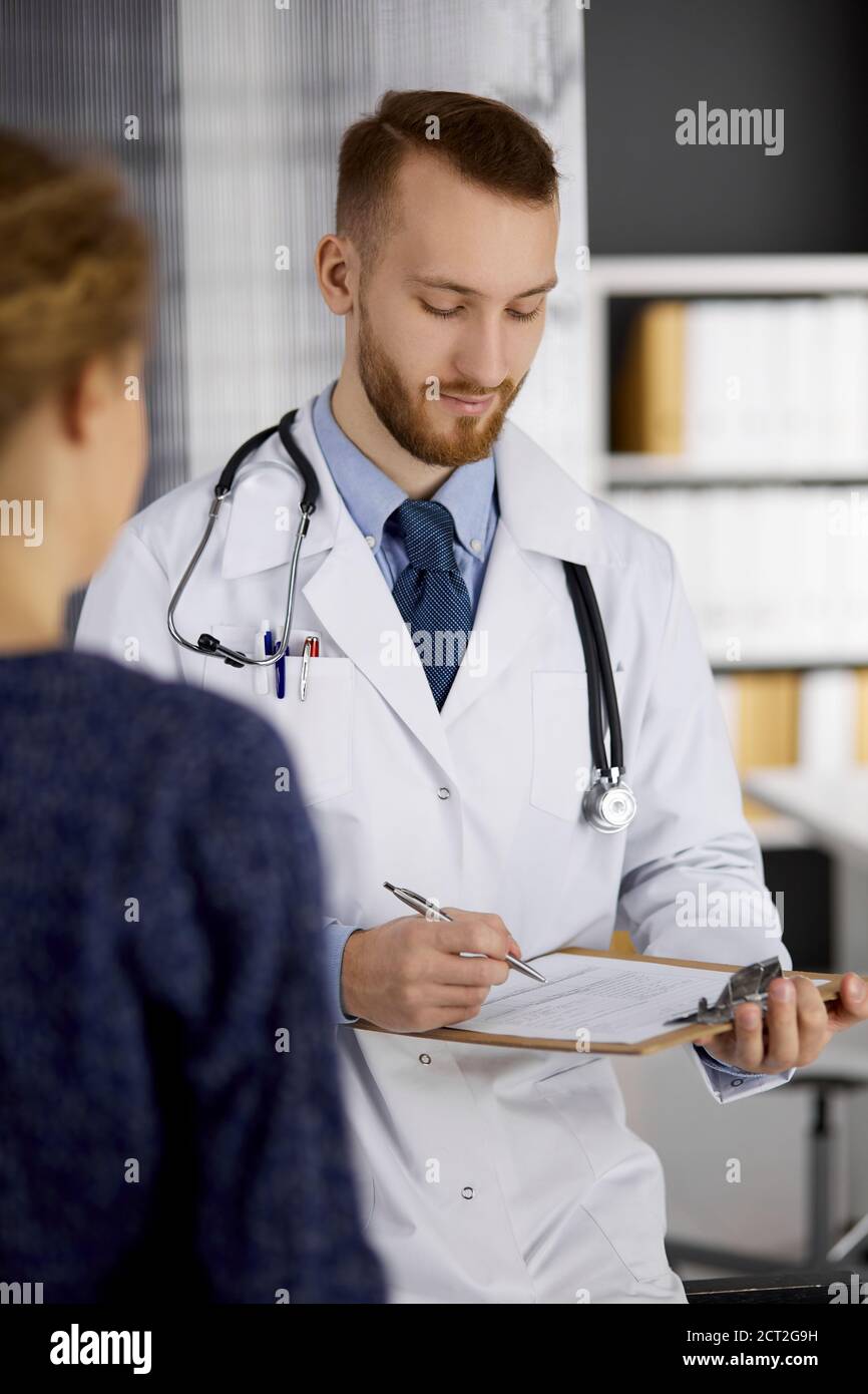 Friendly red-bearded doctor and patient woman discussing current health ...