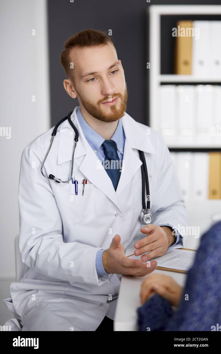 Friendly red-bearded doctor and patient woman discussing current health ...