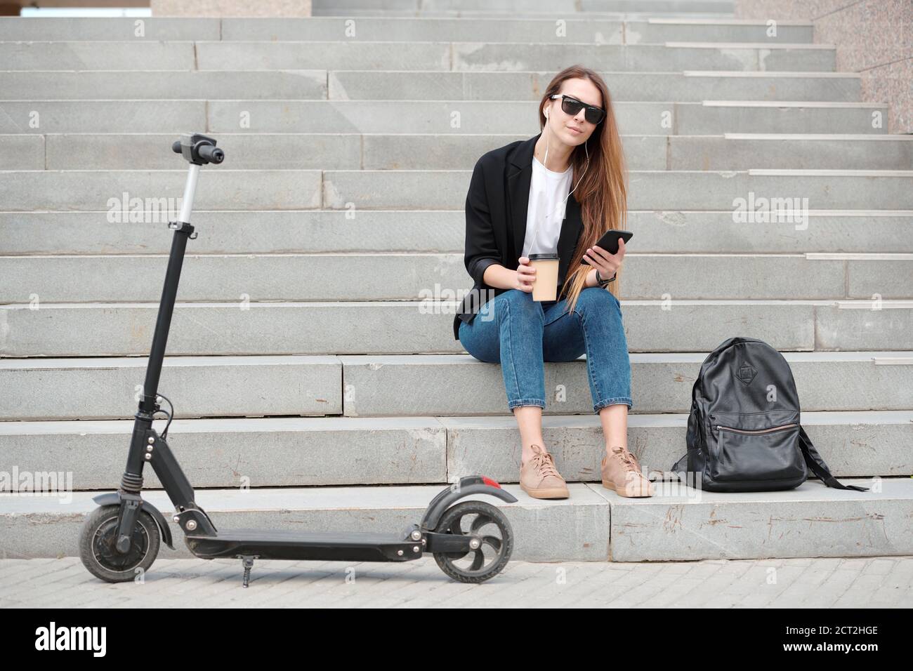 Contemporary female student with glass of coffee sitting on staircase ...