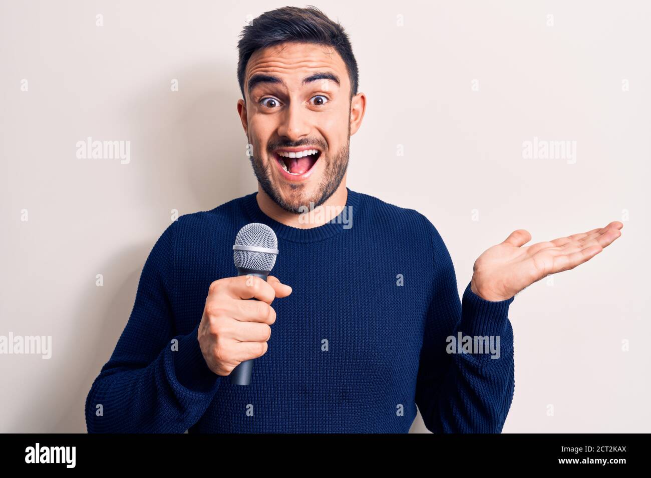 Young handsome singer man with beard singing song using microphone over white background ...