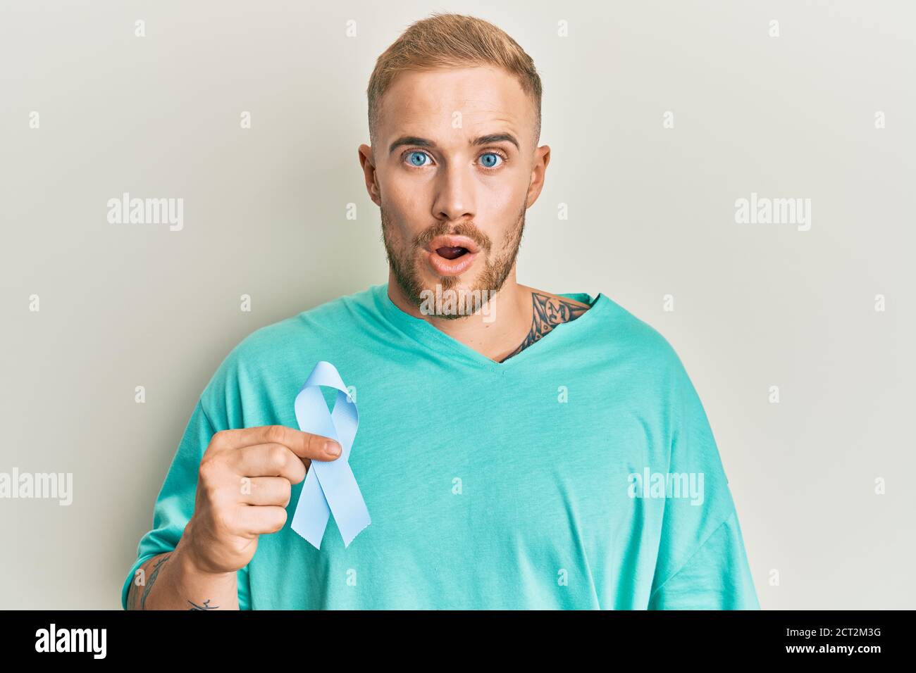 Young caucasian man holding blue ribbon scared and amazed with open ...