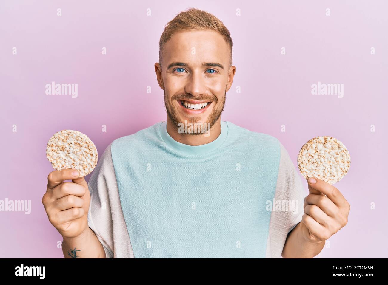 Young caucasian man eating healthy rice crackers smiling with a happy ...