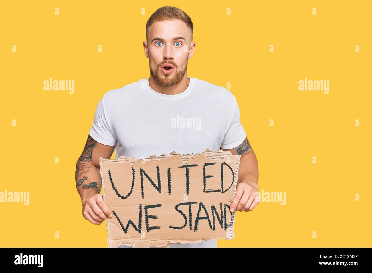 Young irish man holding united we stand banner scared and amazed with ...