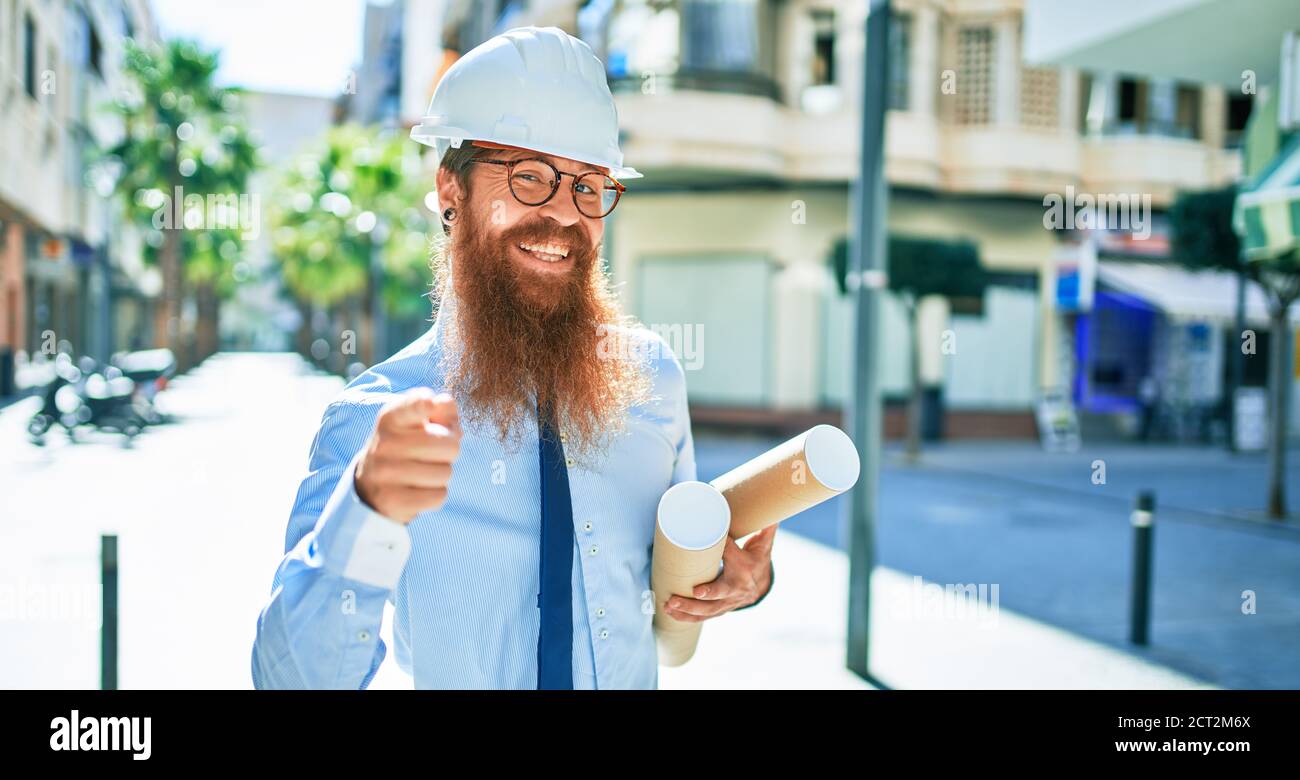 Young redhead architect man with long beard wearing hardhat smiling ...