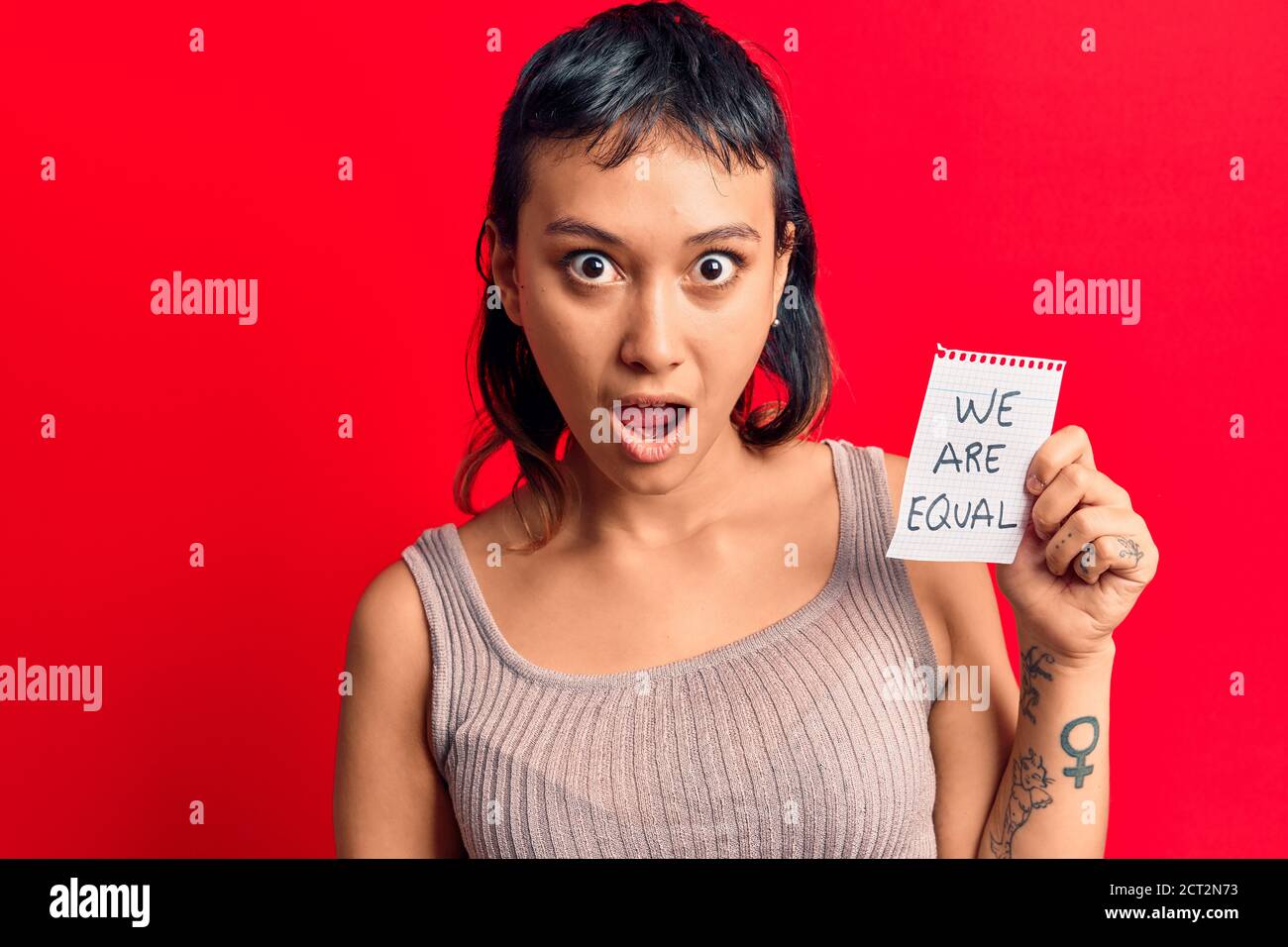 Young woman holding we are equal paper scared and amazed with open ...