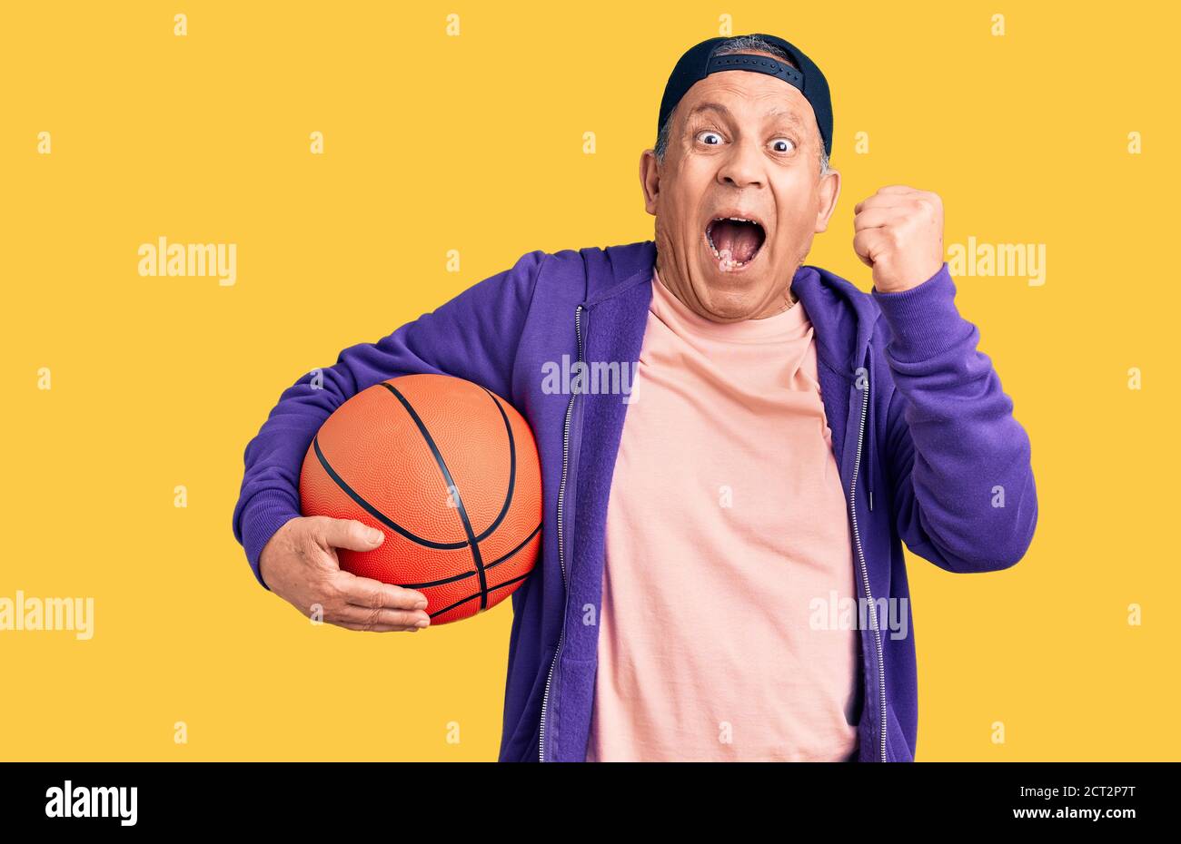 Senior handsome grey-haired man holding basketball ball screaming proud ...
