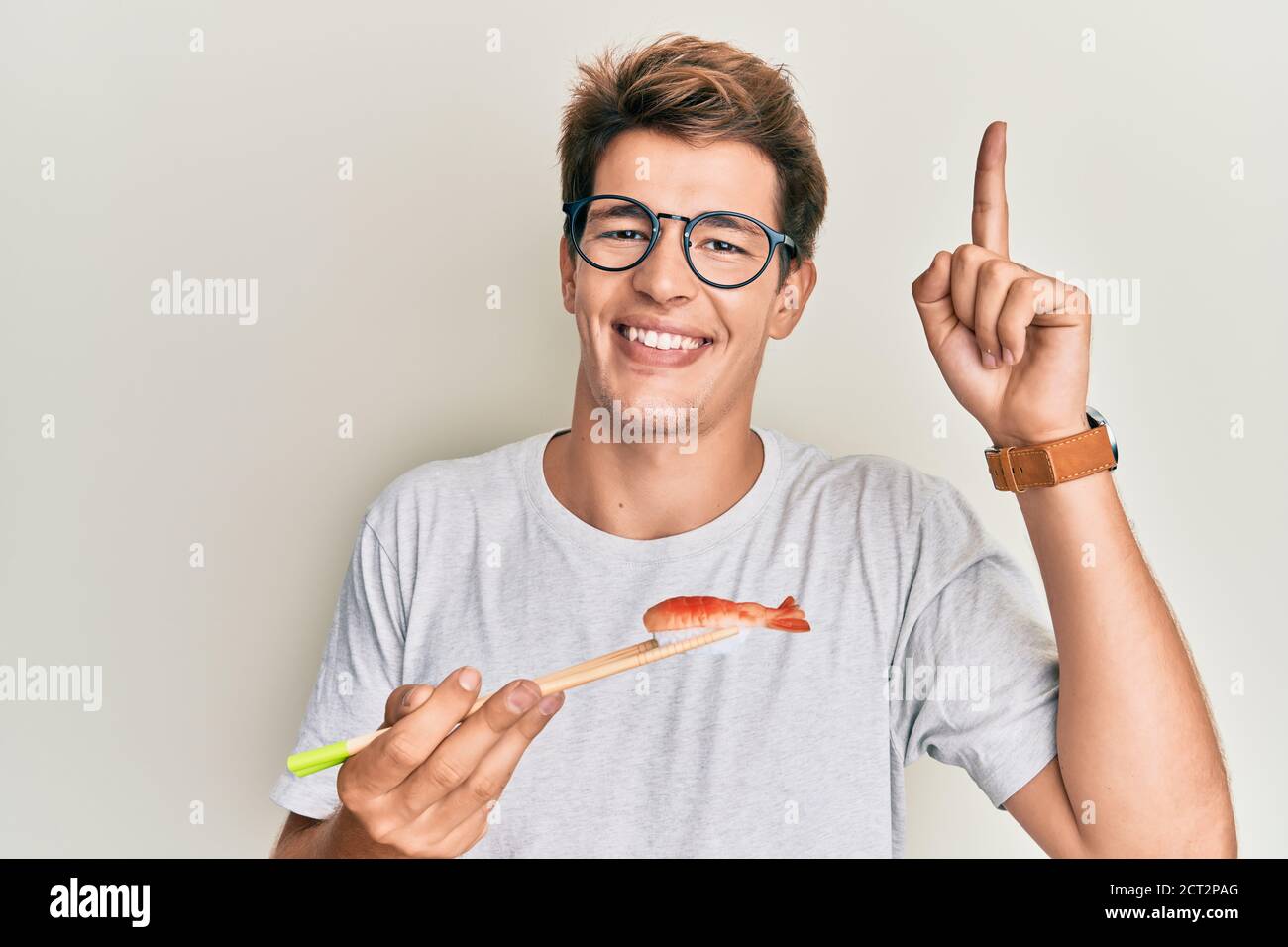 Handsome caucasian man eating prawn sushi using chopsticks smiling with ...