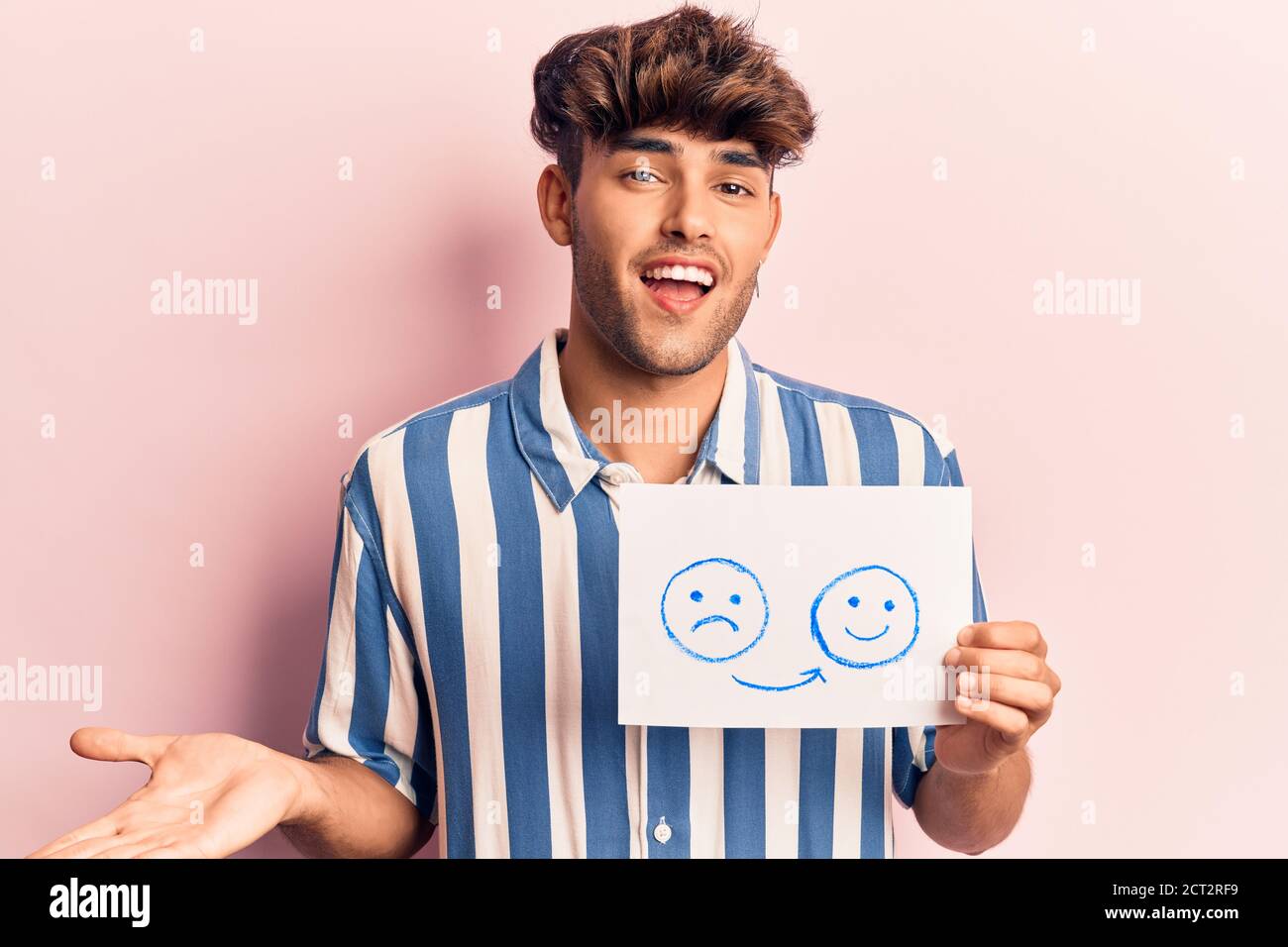 Young hispanic man holding sad to happy emotion paper celebrating ...