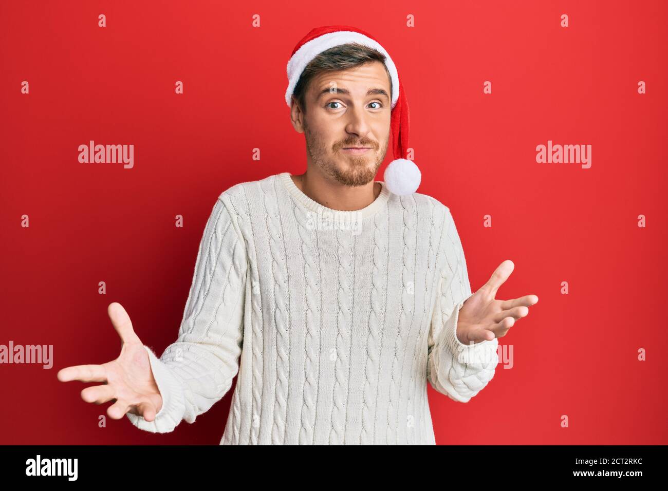 Handsome caucasian man wearing christmas hat clueless and confused ...