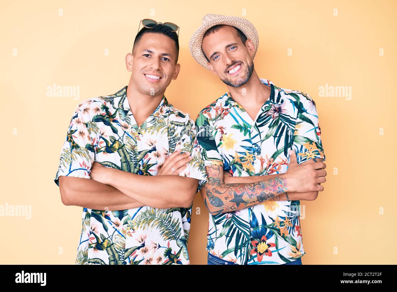 Young gay couple of two men wearing summer hat and hawaiian shirt happy ...