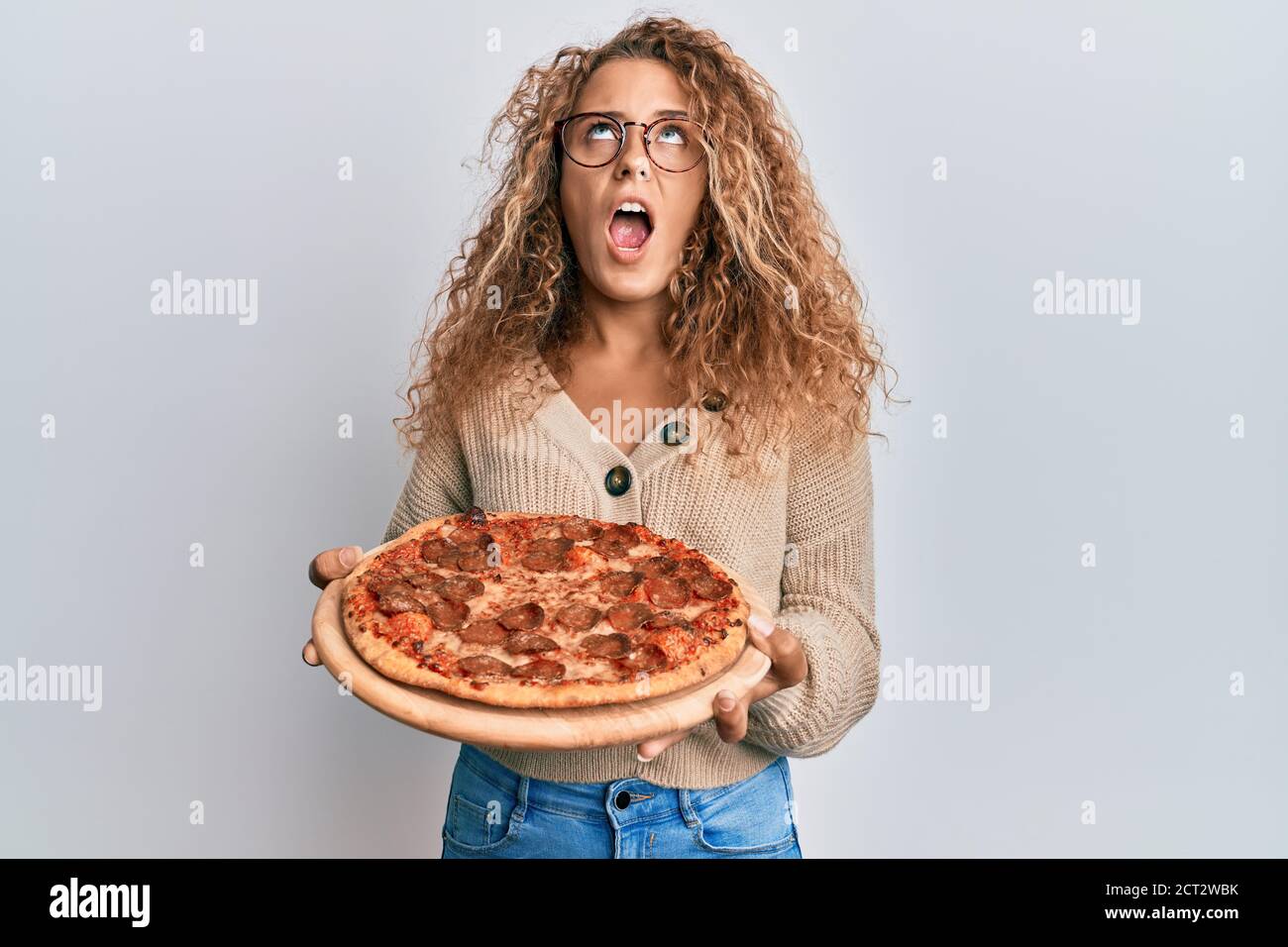 Beautiful caucasian teenager girl eating tasty pepperoni pizza angry ...