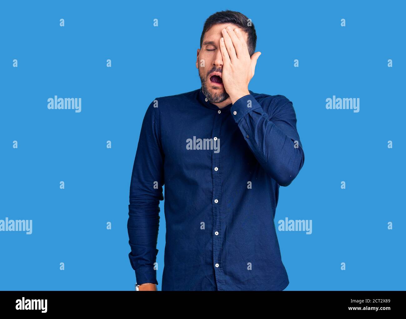 Young handsome man wearing casual shirt yawning tired covering half ...