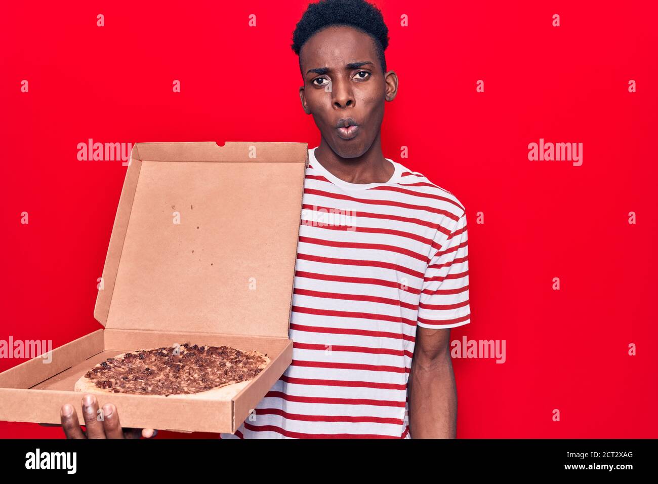 Young african american man holding delivery pizza box scared and amazed ...
