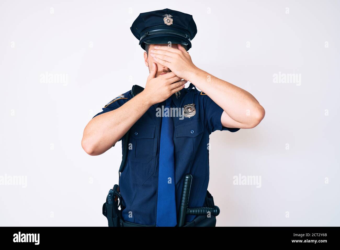 Young caucasian man wearing police uniform covering eyes and mouth with ...