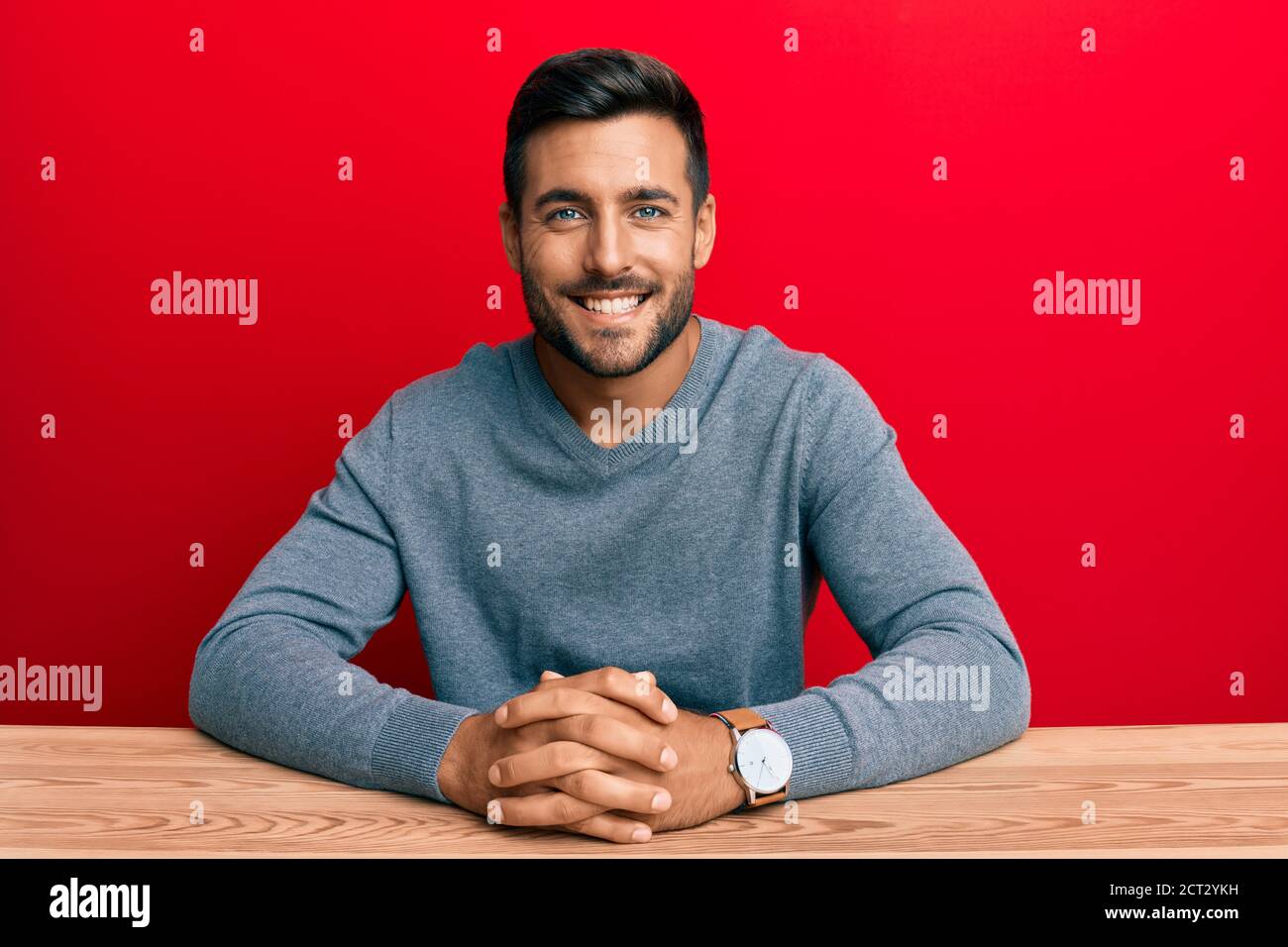 Handsome hispanic man wearing casual style sitting on the table with a ...
