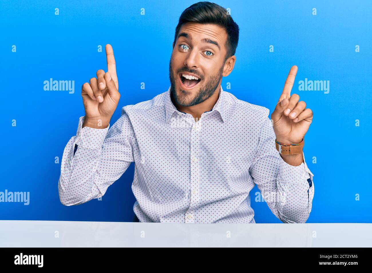 Handsome hispanic man wearing business clothes sitting on the table ...
