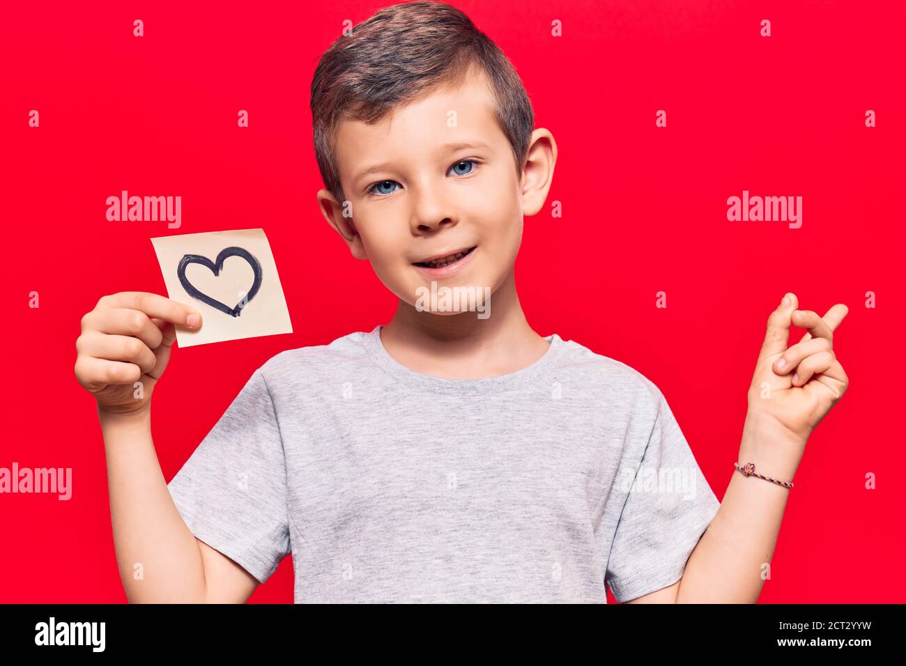 Cute blond kid holding heart reminder smiling happy pointing with hand ...