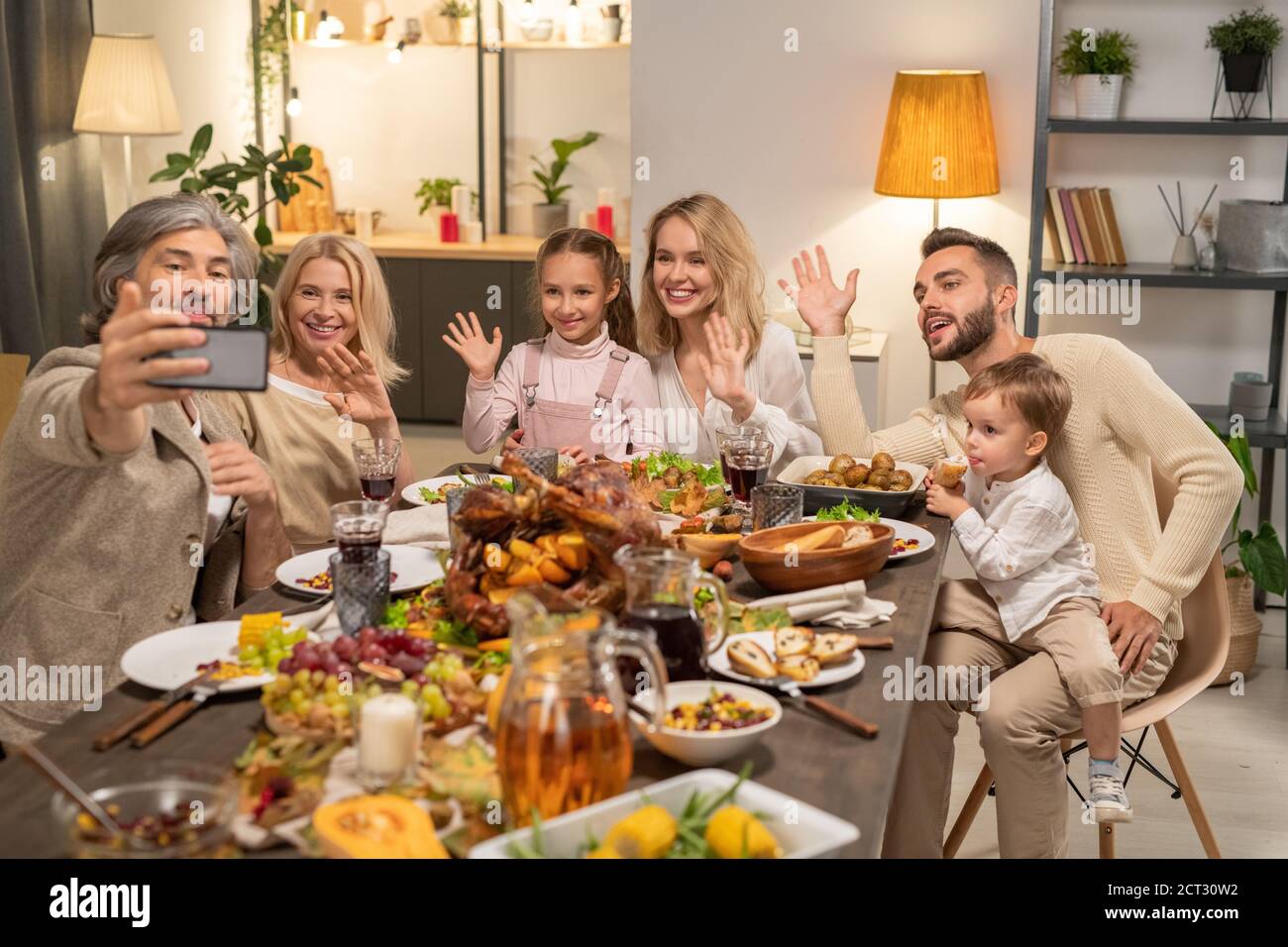 Happy large family of three generations waving hands by festive table ...