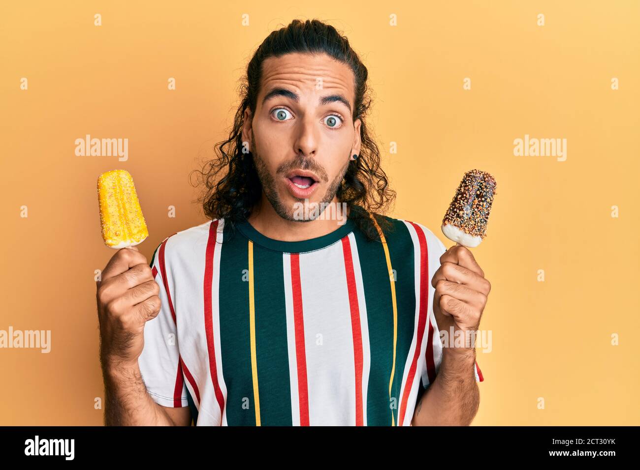 Young handsome man with long hair eating two ice cream afraid and ...