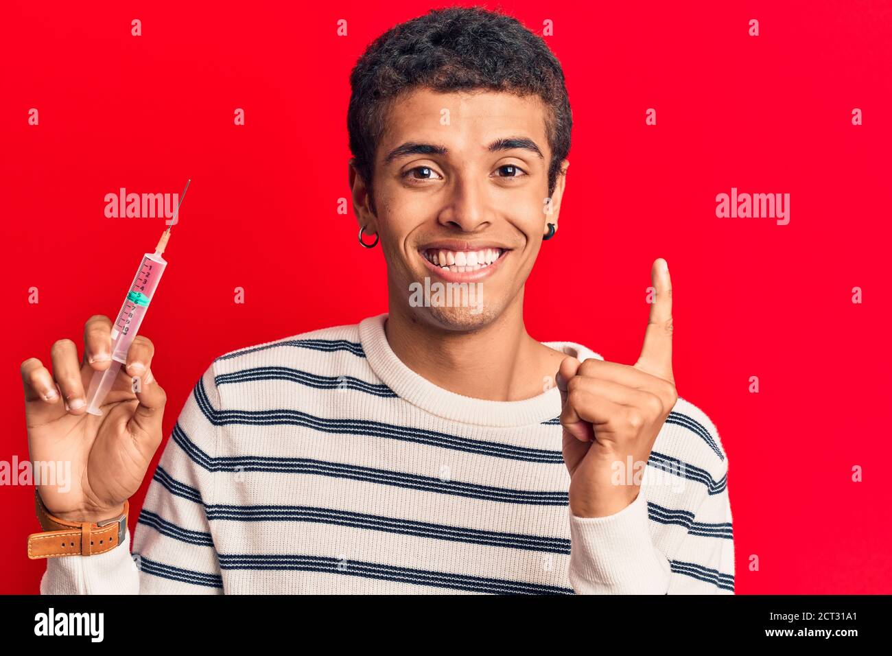 Young african amercian man holding syringe smiling with an idea or question pointing finger with ...