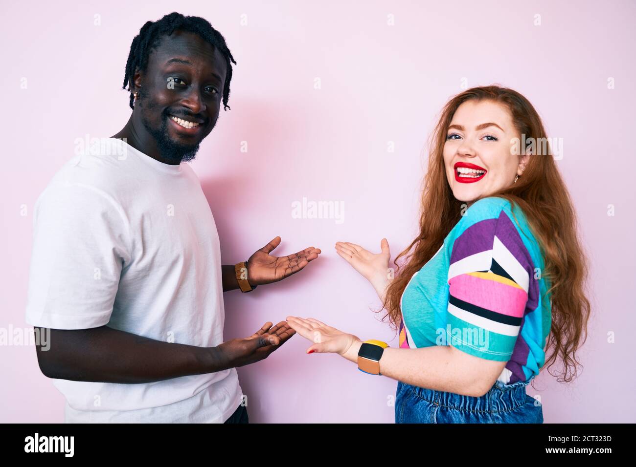Interracial Couple Wearing Casual Clothes Inviting To Enter Smiling