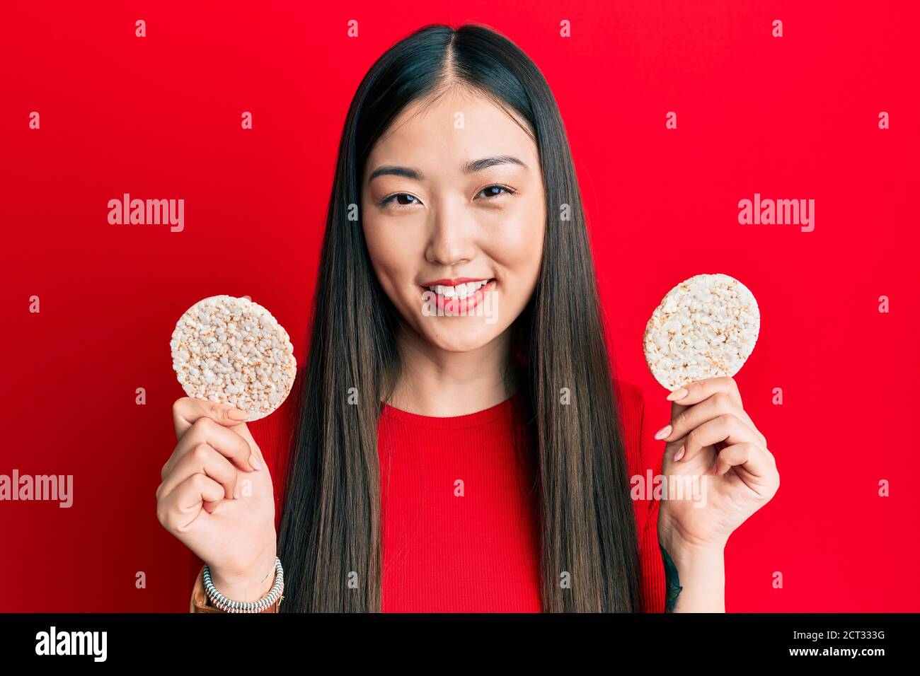 Young chinese woman eating healthy rice crackers smiling with a happy ...