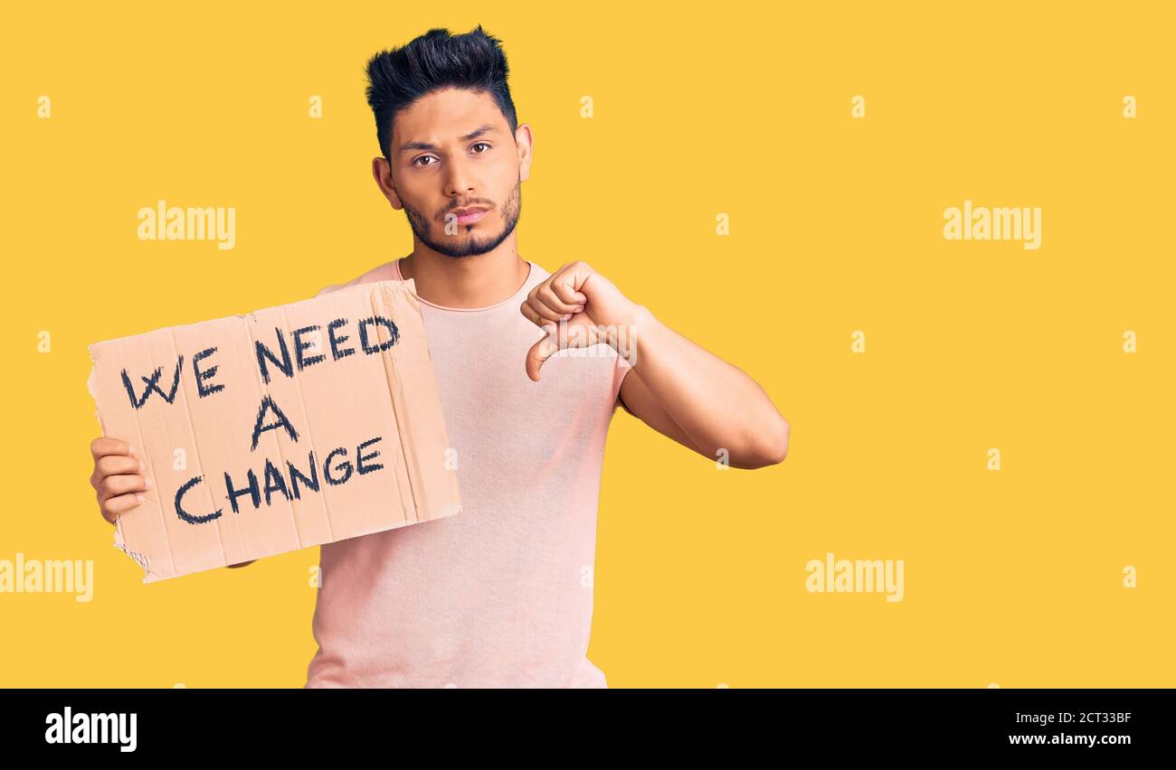 Handsome latin american young man holding we need a change banner with ...