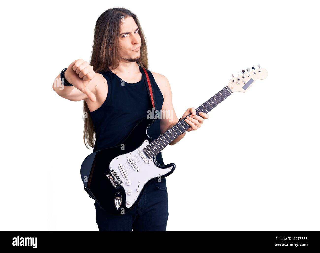 Young adult man with long hair playing electric guitar with angry face ...
